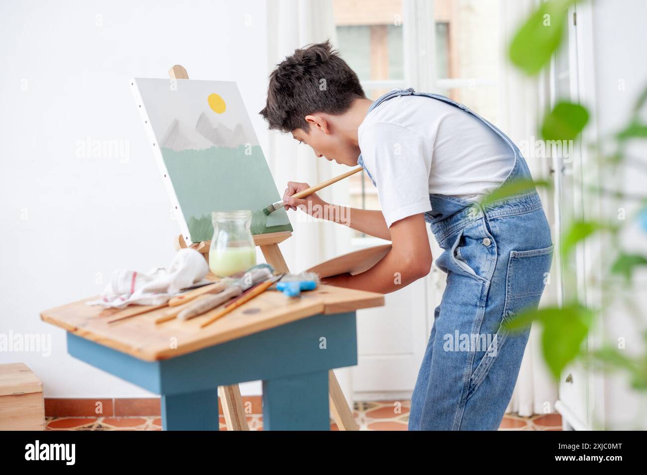 A teenager is painting a landscape with a paintbrush on a canvas on an ...