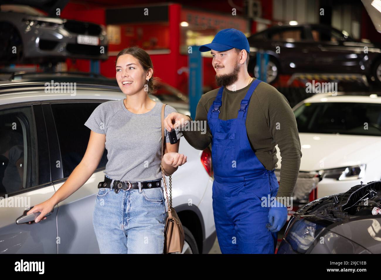 Kind car mechanic handing over the keys of car to glad female client in ...