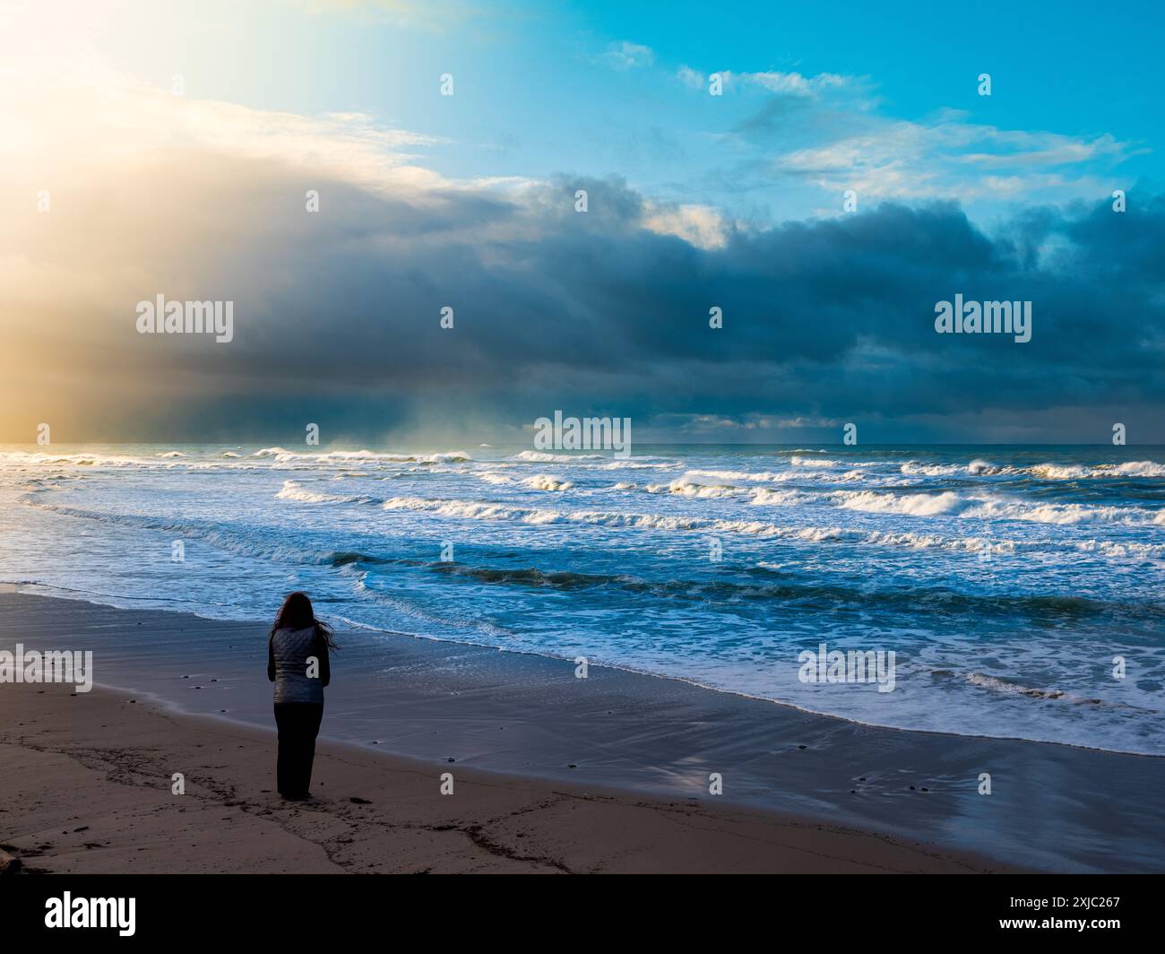 Woman looking out to sea in dramatic ocean beach scene Stock Photo - Alamy