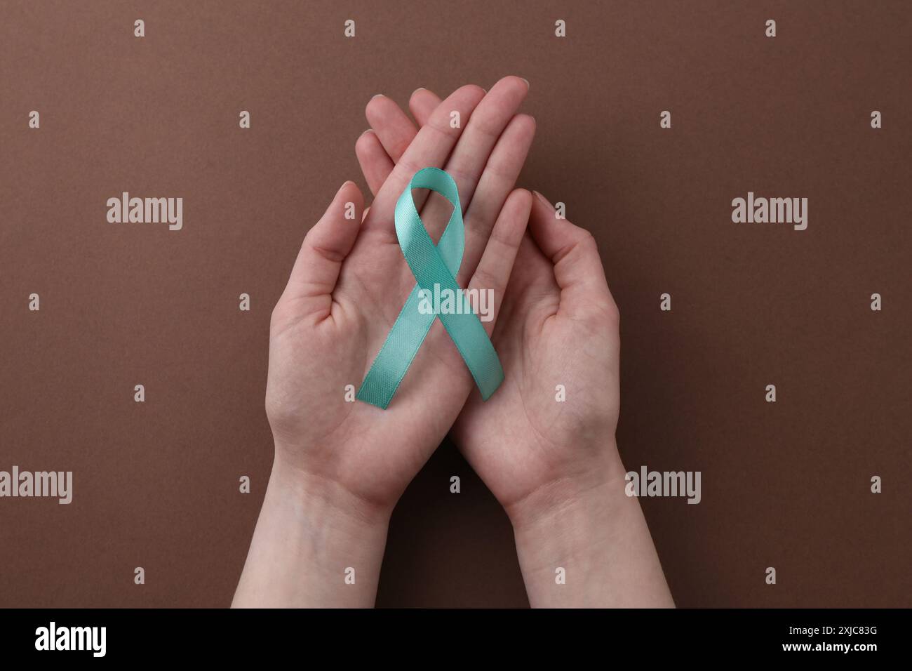 Woman holding turquoise awareness ribbon on brown background, top view ...