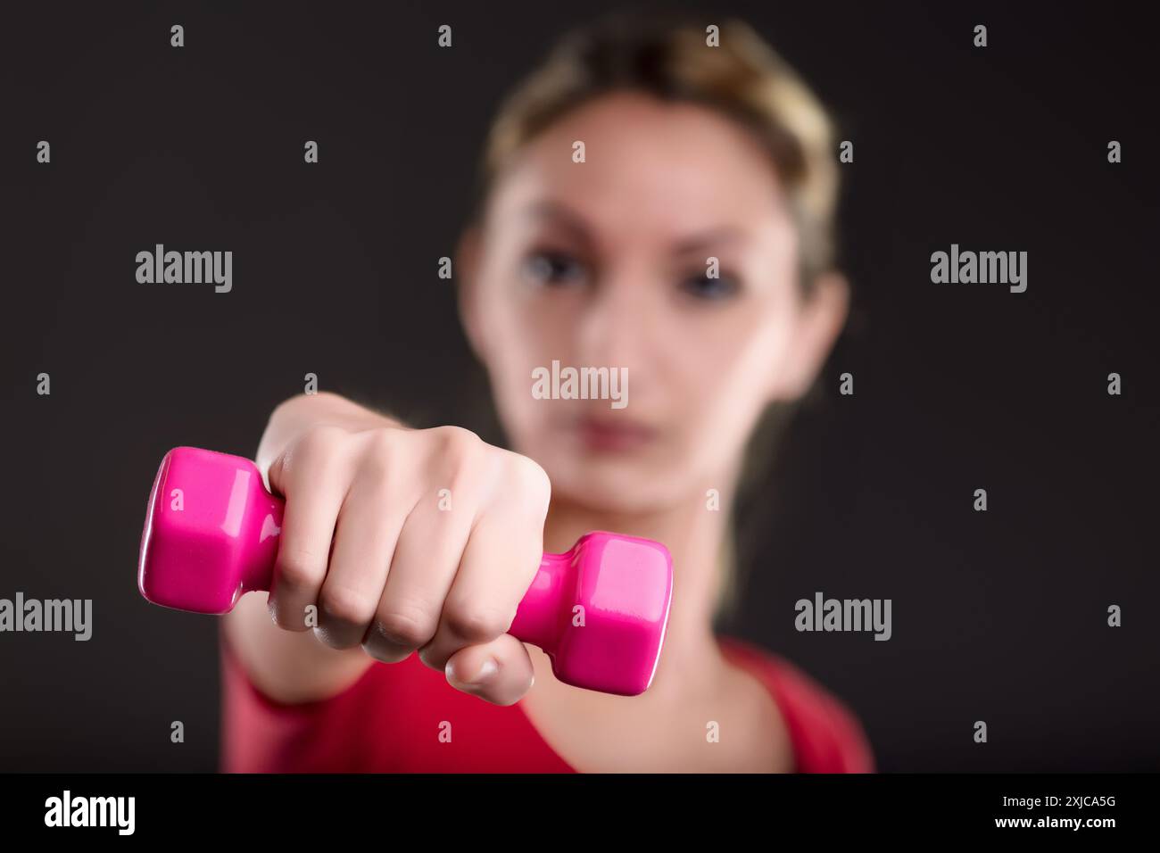 Young woman lifting a pink dumbbell, showing determination and strength ...