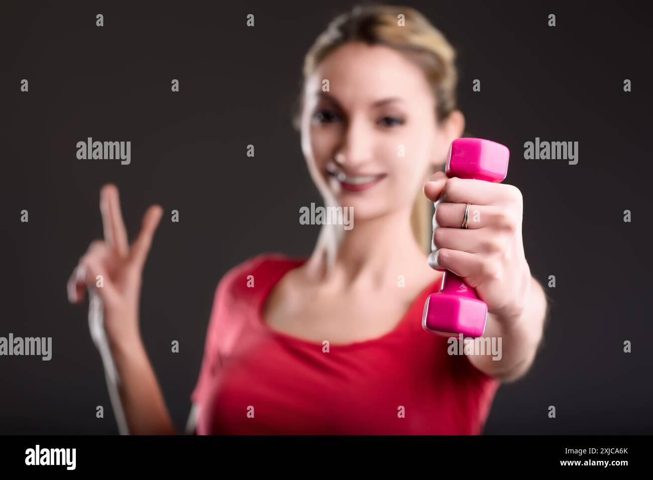 Young woman is holding a dumbbell and making the victory sing while ...