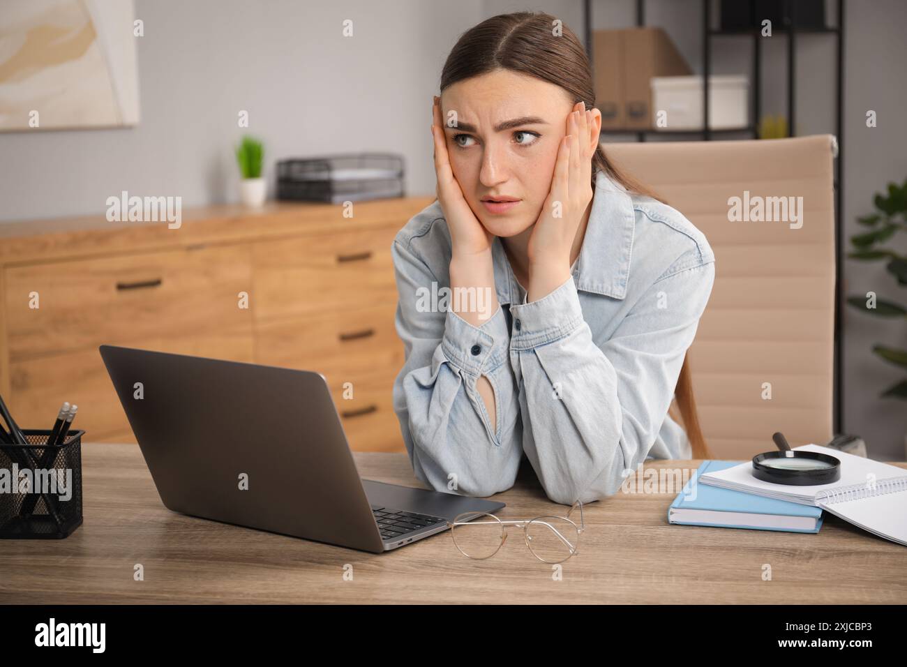 Embarrassed woman at wooden table with laptop in office Stock Photo - Alamy