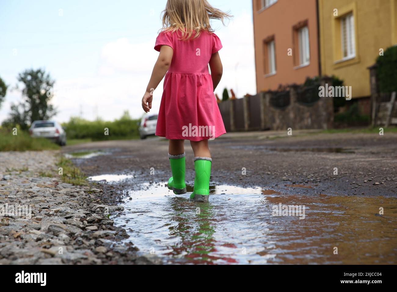 Little girl wearing green rubber boots walking in puddle outdoors, back ...