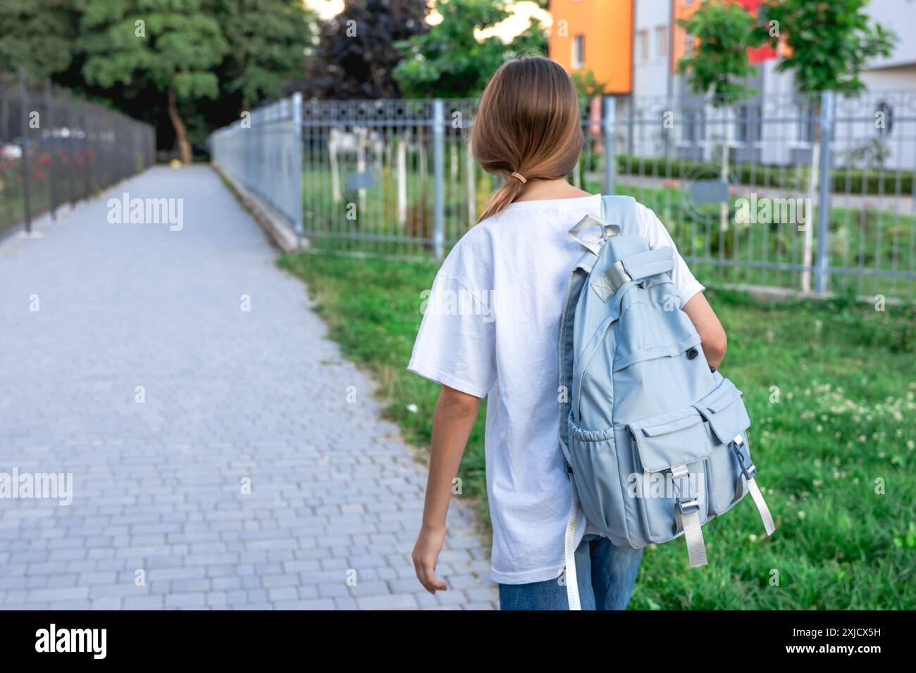 Schoolgirl walks near school. A girl with a backpack on her shoulders ...