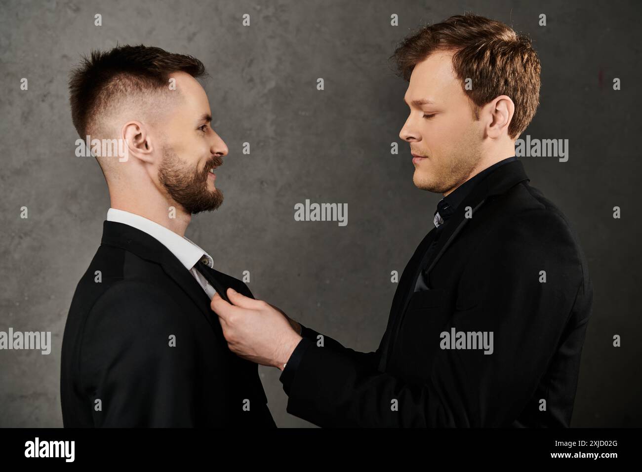 Two men in elegant suits stand close, one adjusting the others tie ...
