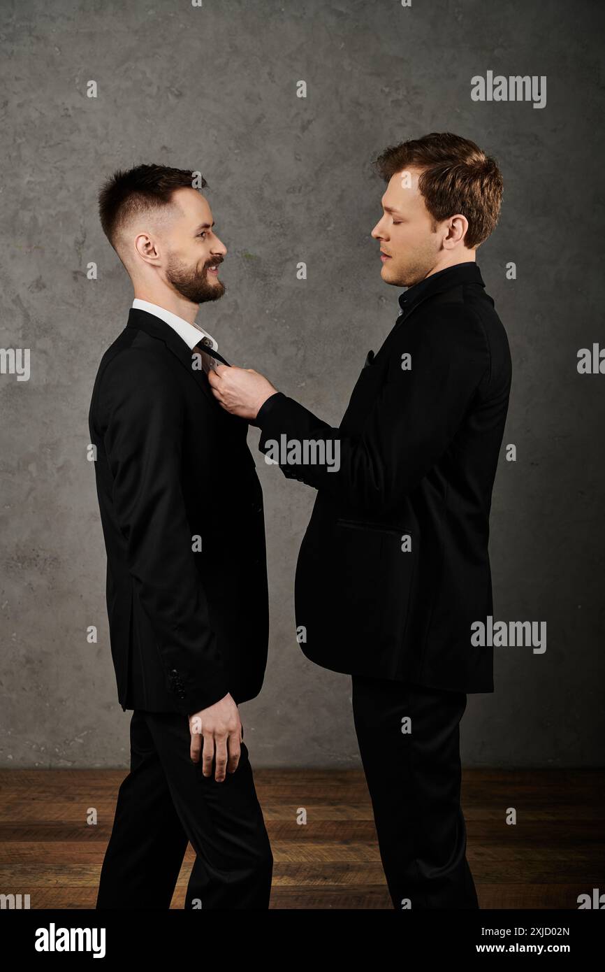 A dapper couple in black suits, one adjusting the others tie, standing ...