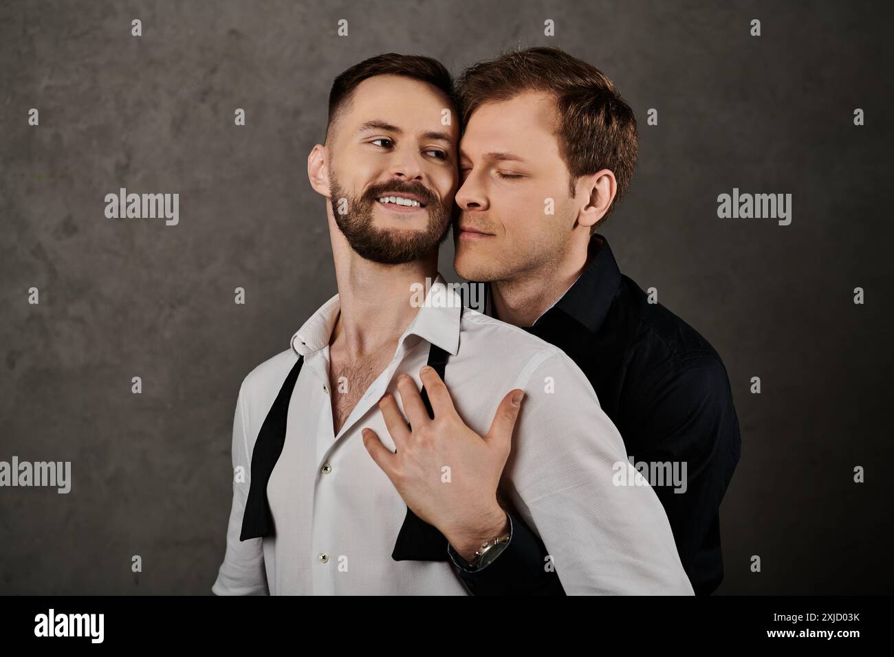 Two men in elegant suits stand close, one embracing the other with a ...
