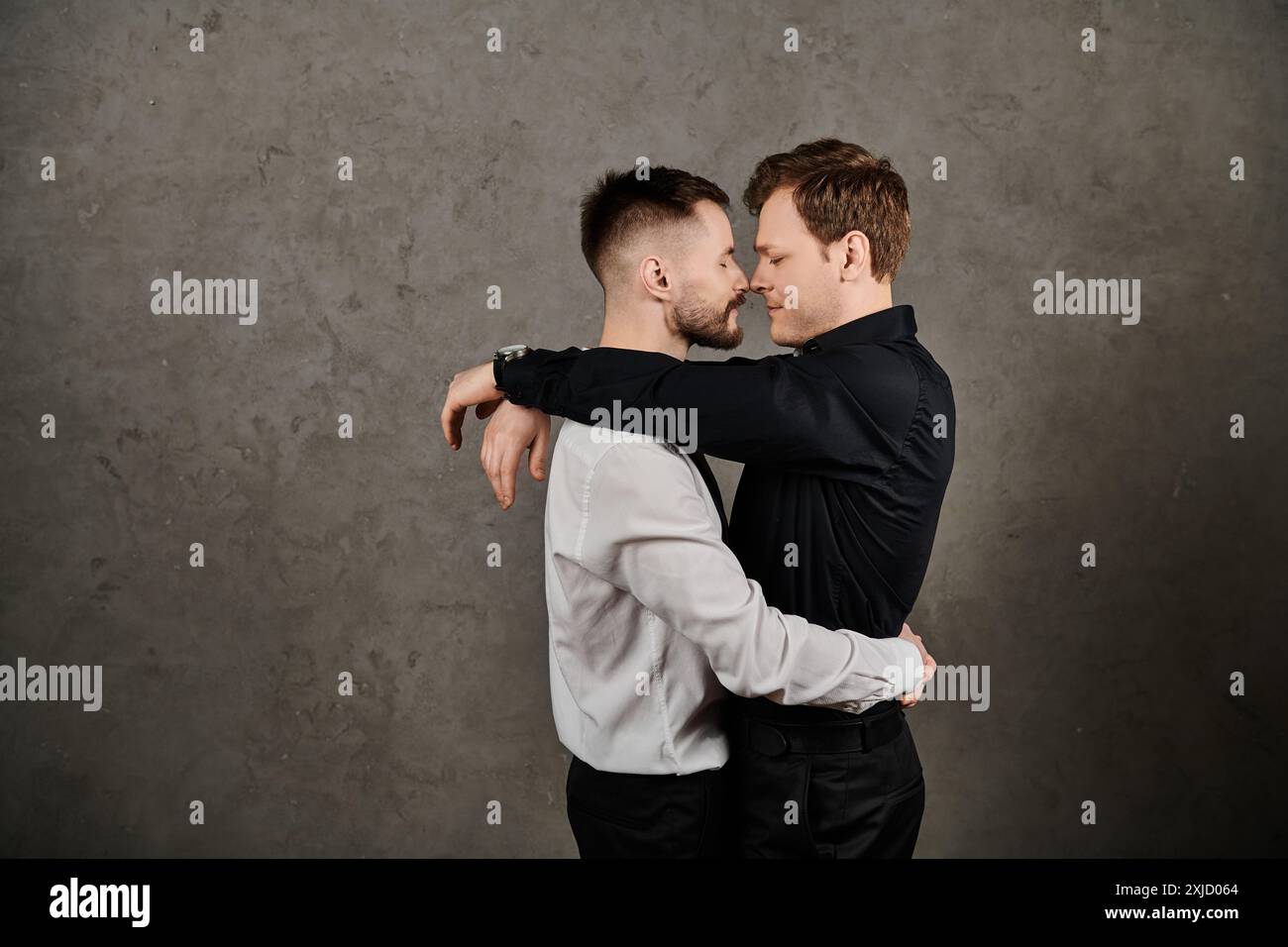 Two men in suits embrace passionately against a textured concrete wall ...