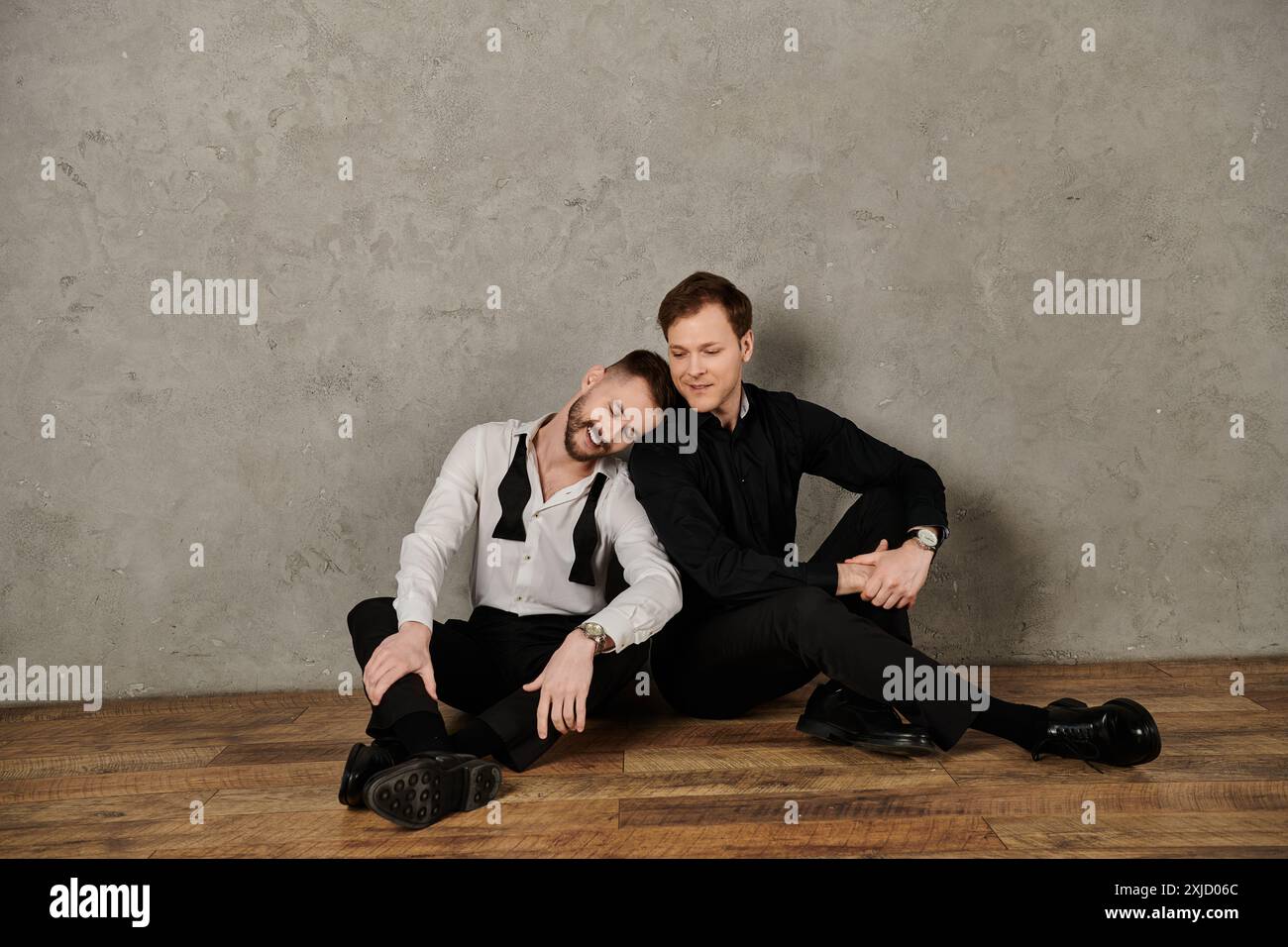 Two men in elegant suits share a tender moment, leaning against each ...