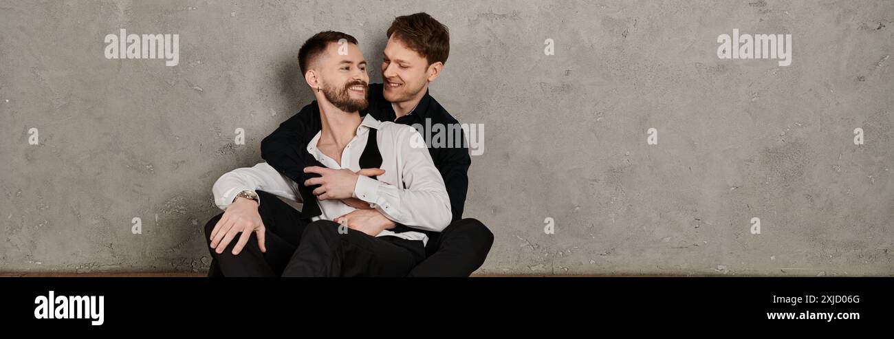 Two men in elegant suits share a loving embrace against a concrete ...