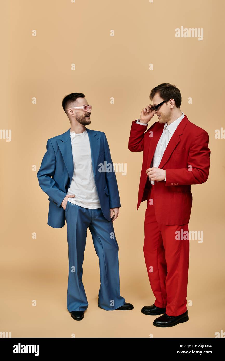 Two men in suits, one in blue and one in red, pose against a beige ...