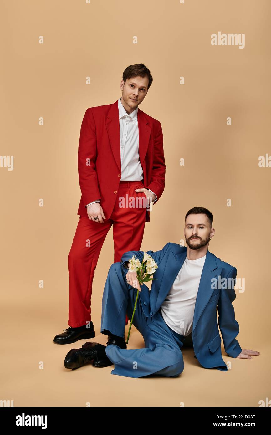 Two men in elegant suits pose: one in red standing tall, the other in ...
