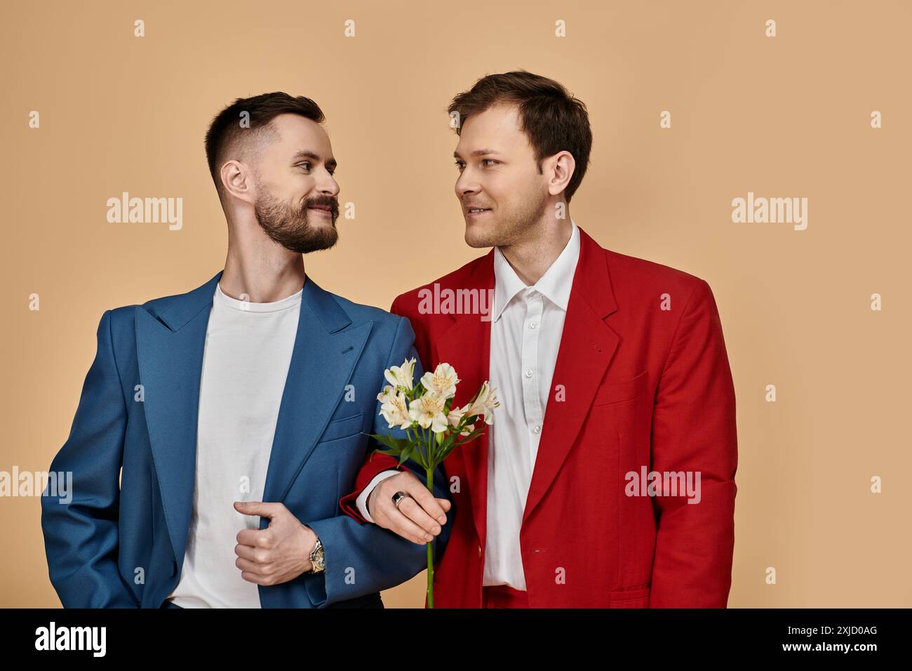 Two men in stylish suits look lovingly at each other against a soft ...