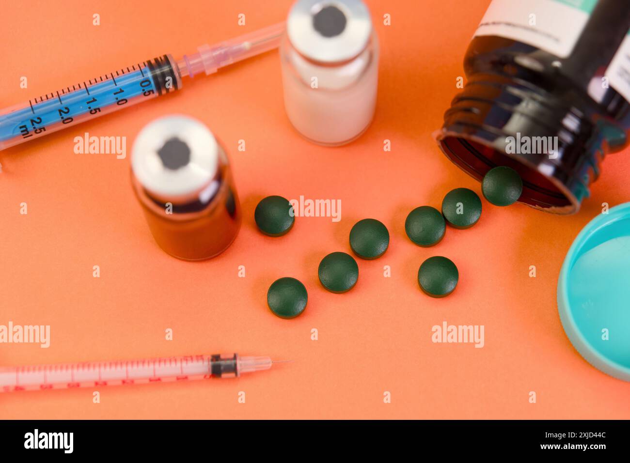 Green tablets spilled from a bottle alongside syringes and vials on a ...