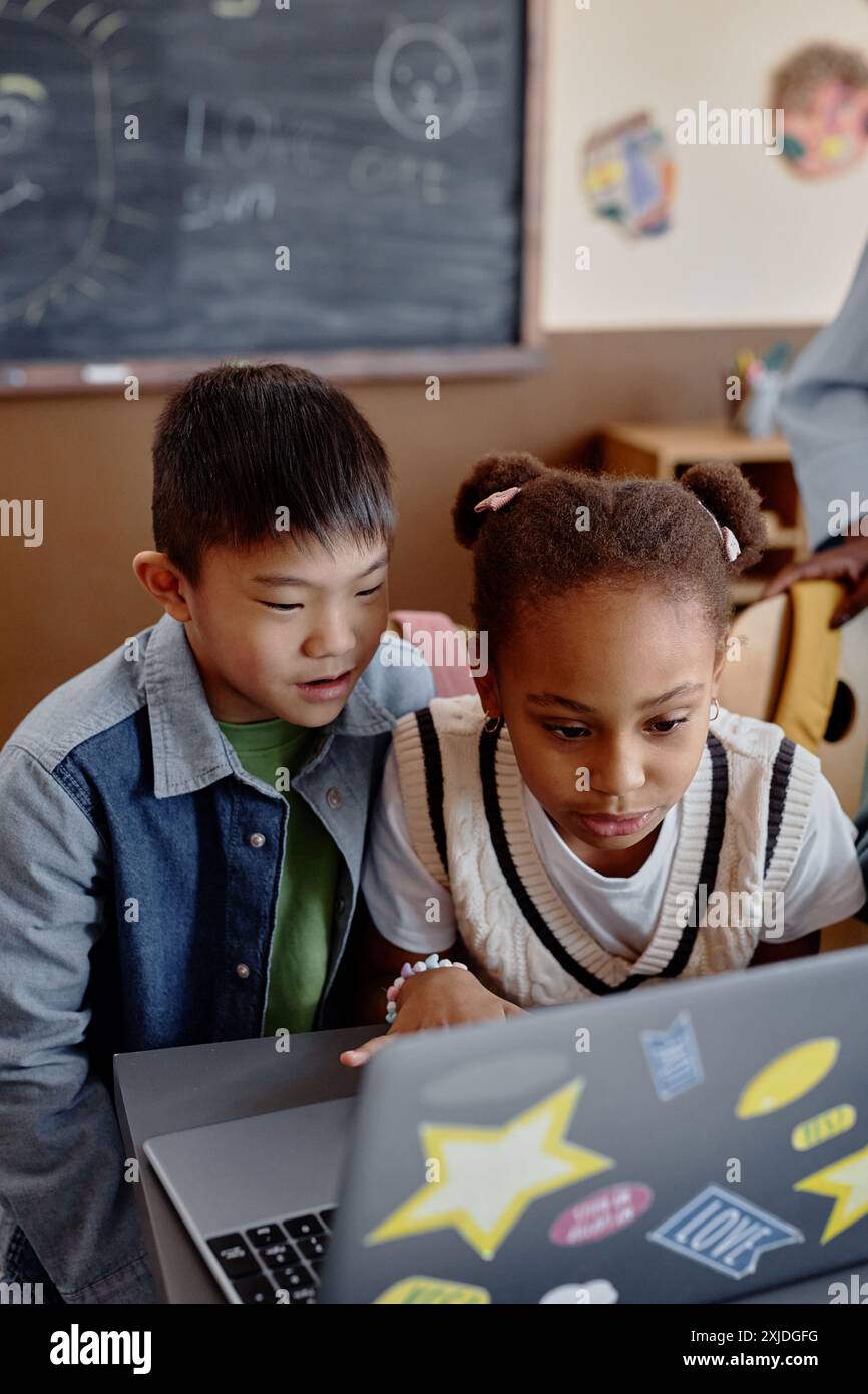 Vertical shot of two interested kids looking at laptop screen engaged ...