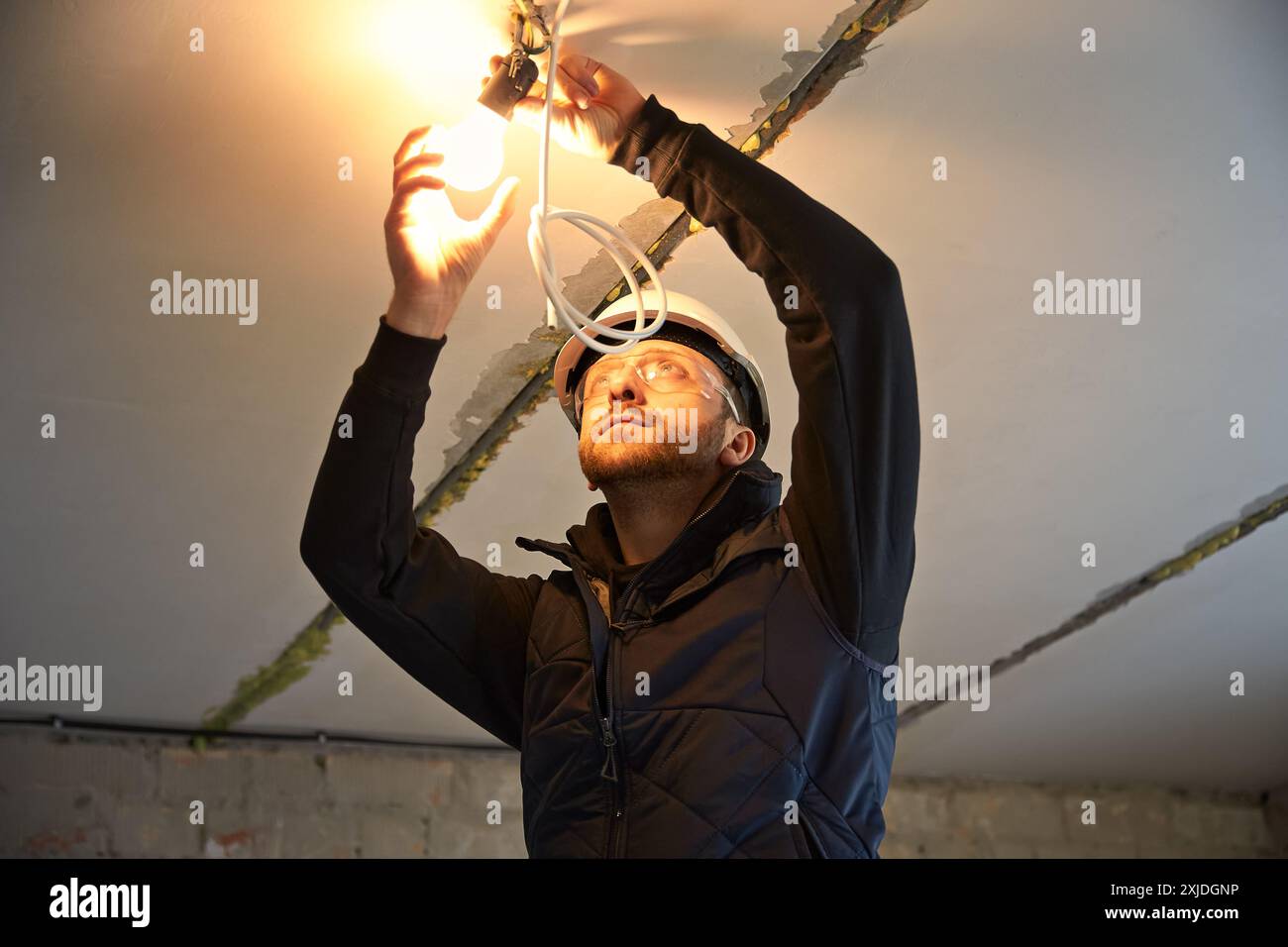 Male construction worker installing temporary light bulb on the ceiling ...