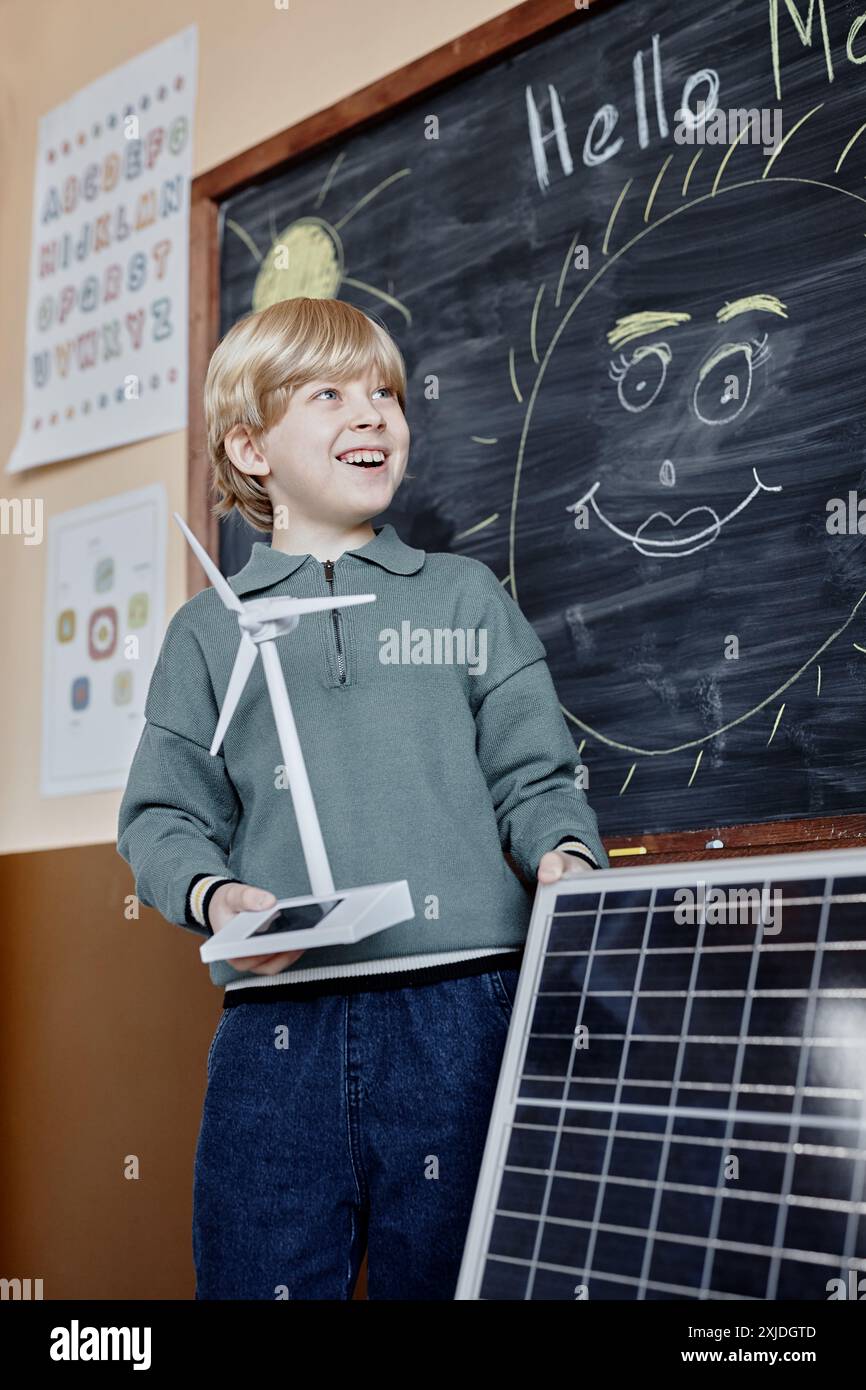 Vertical shot of cheerful primary learner presenting green energy ...