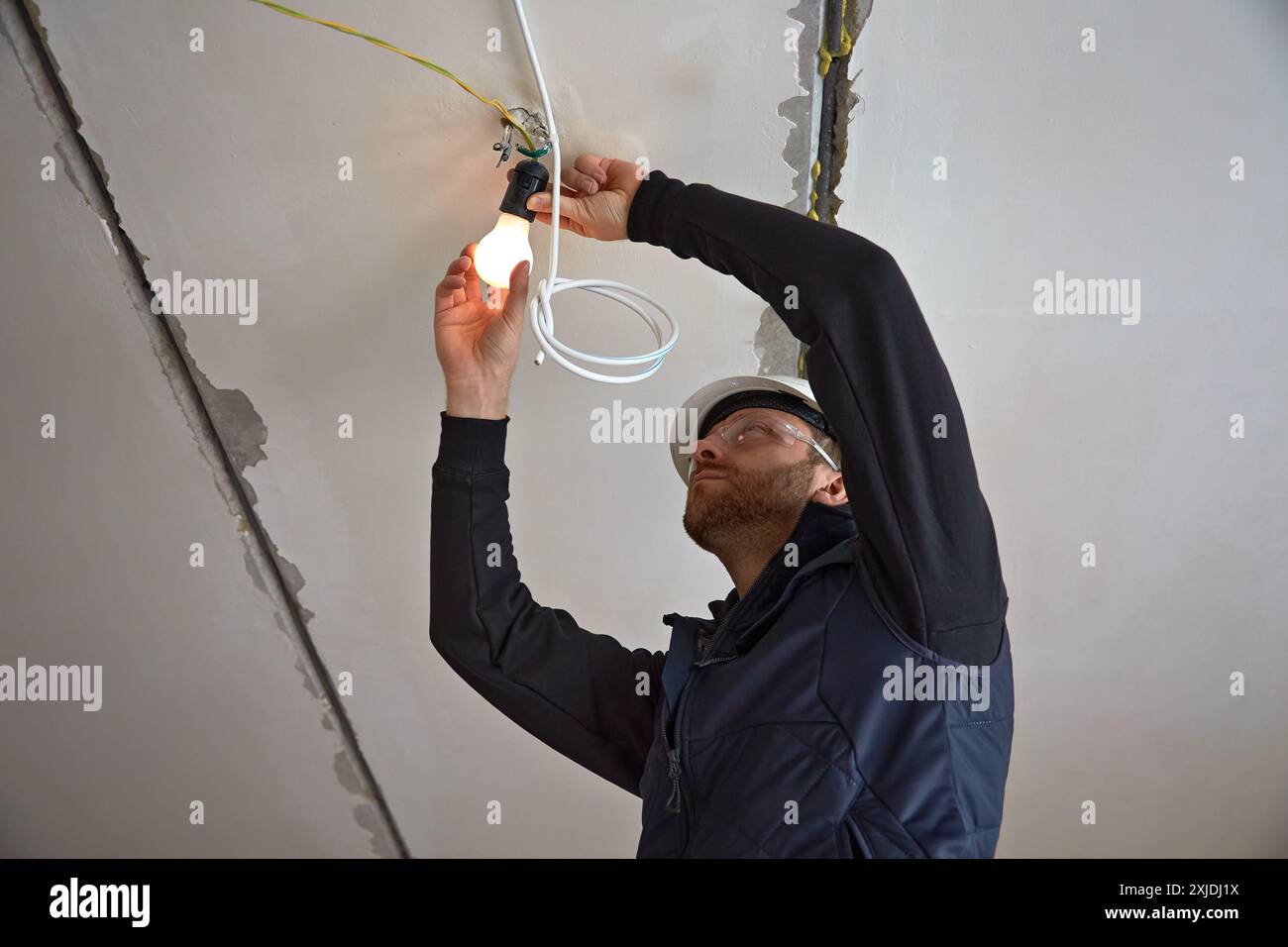 Portrait of male electrician, focused on wiring a temporary light bulb ...