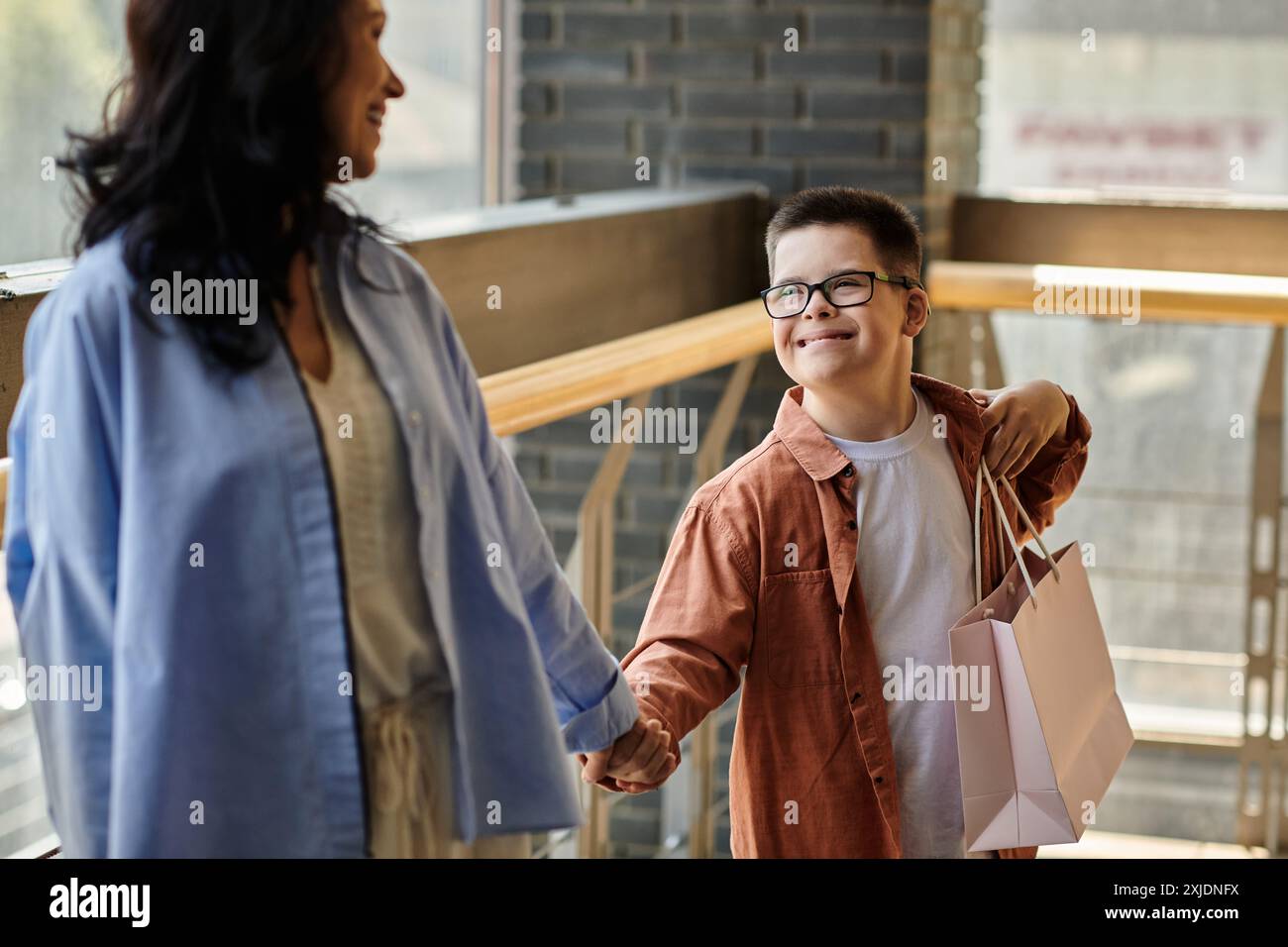 A mother and her son with Down syndrome walk hand-in-hand through a shopping mall, enjoying a ...