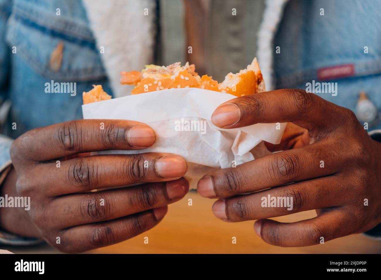 Black man holding and eating a burger wrapped in paper, capturing a ...