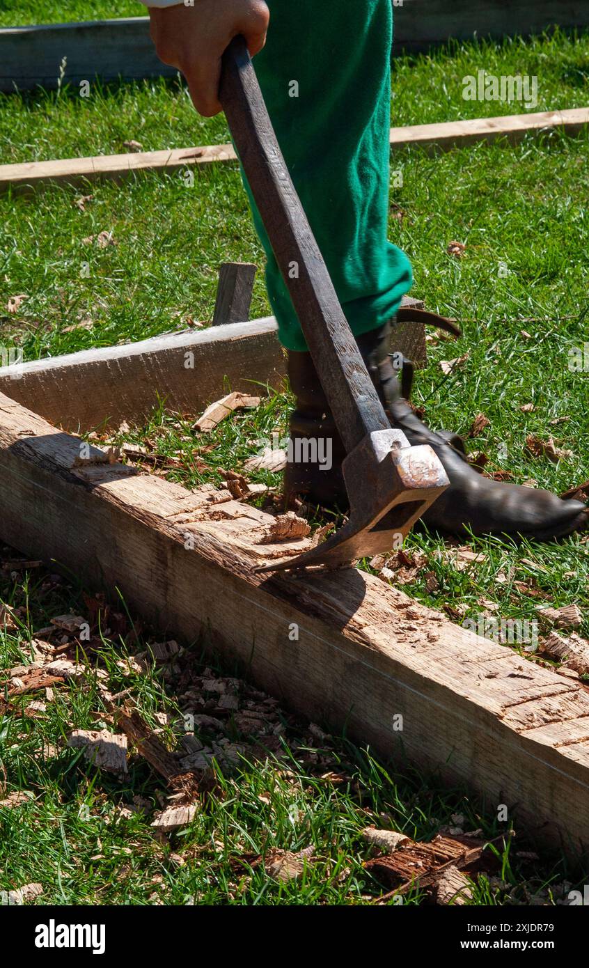 A man using an historic woodworking axe to shape a wooden beam at the ...