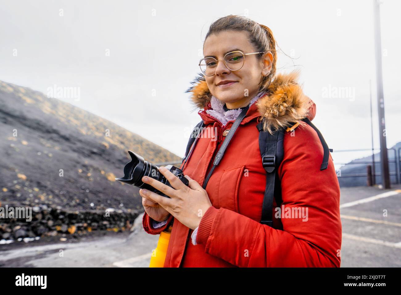 Young woman with camera wearing glasses and red parka jacket on ...