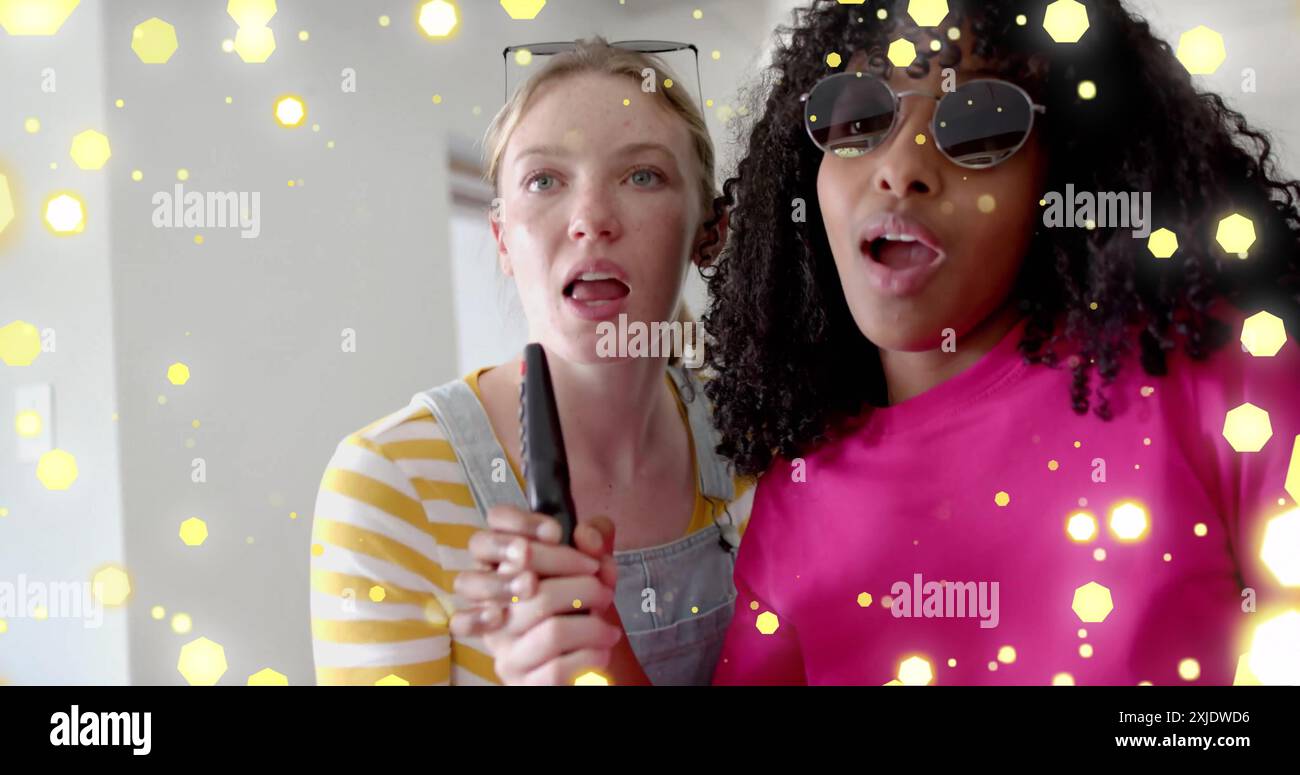 Image of yellow lights over two diverse teenage girls miming singing ...