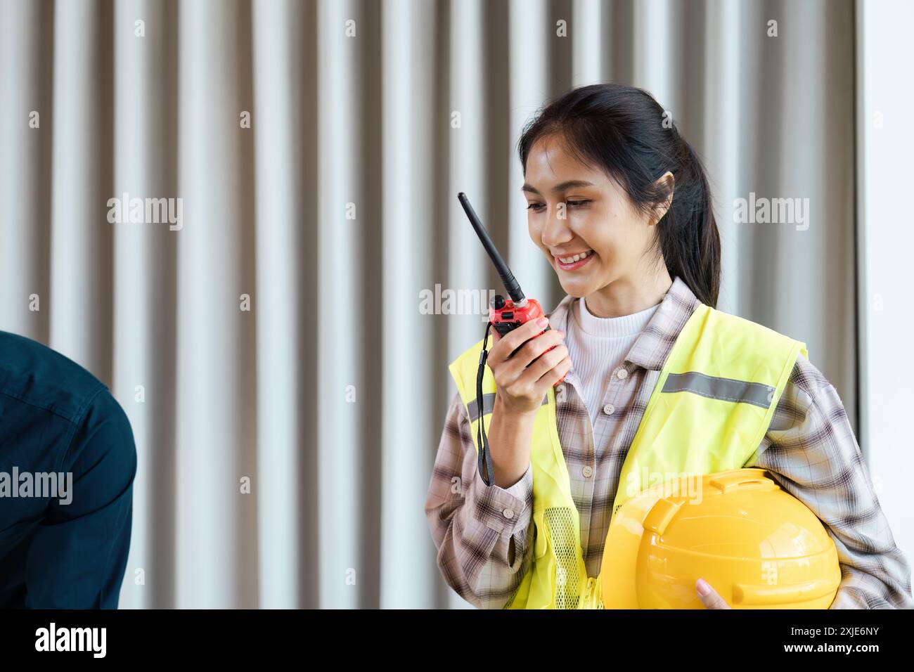 Female Engineer Communicating with Walkie-Talkie and Holding Safety Helmet at Construction Site ...