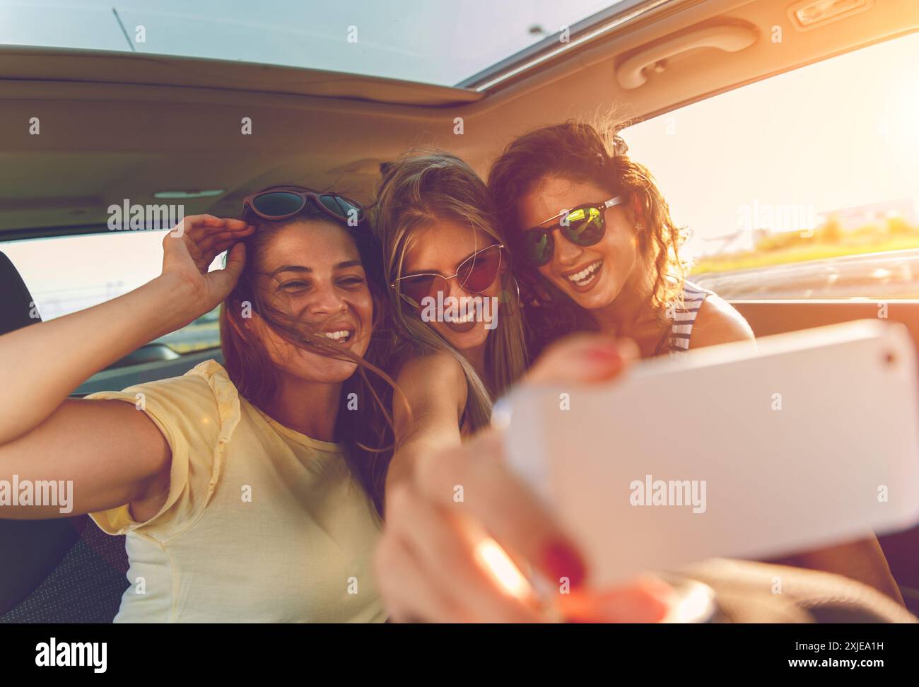 Three female friends enjoying traveling in the car. Sitting in rear ...