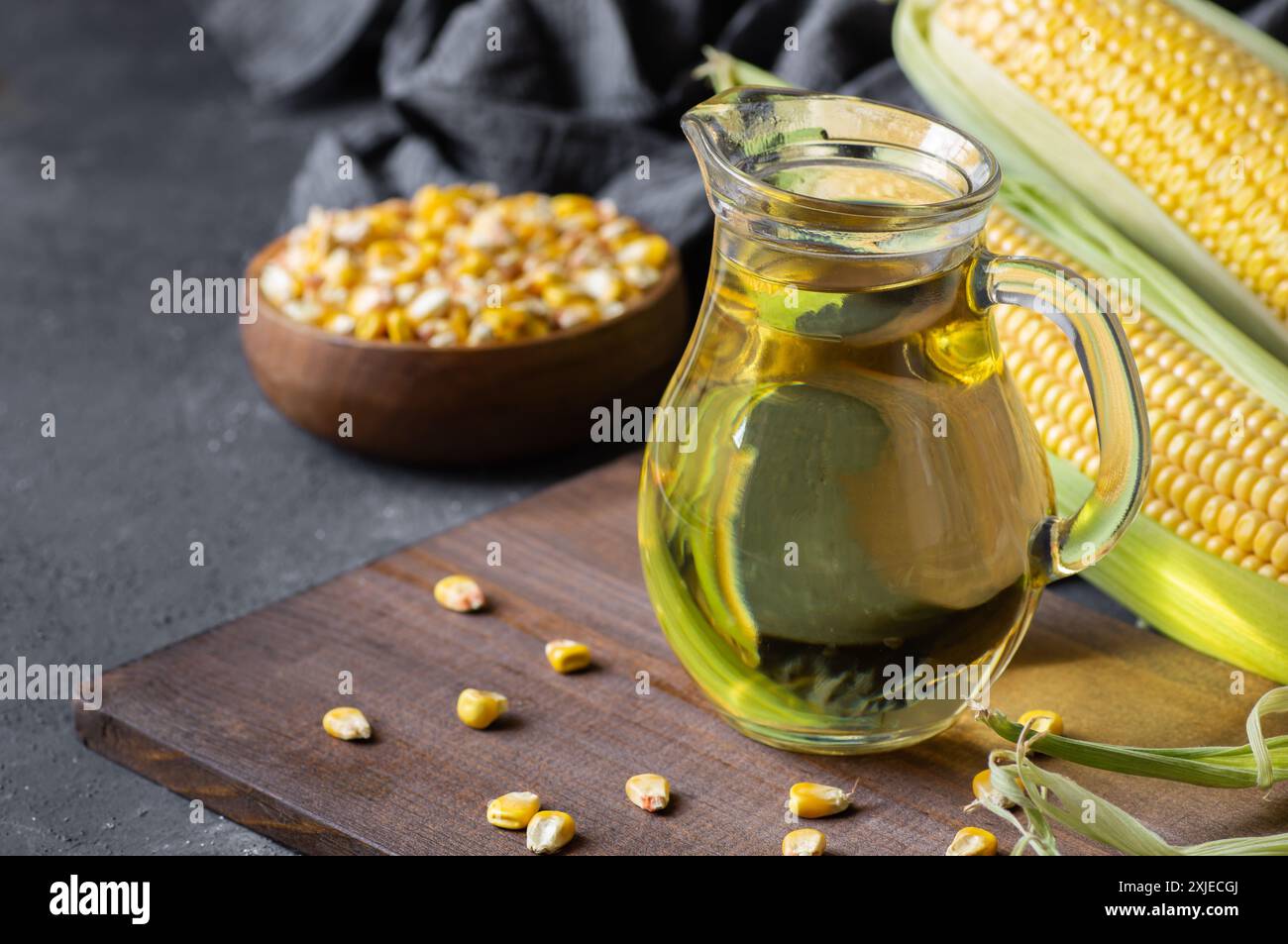 Corn oil in glass bowl with fresh ripe corn cobs on rustic table ...
