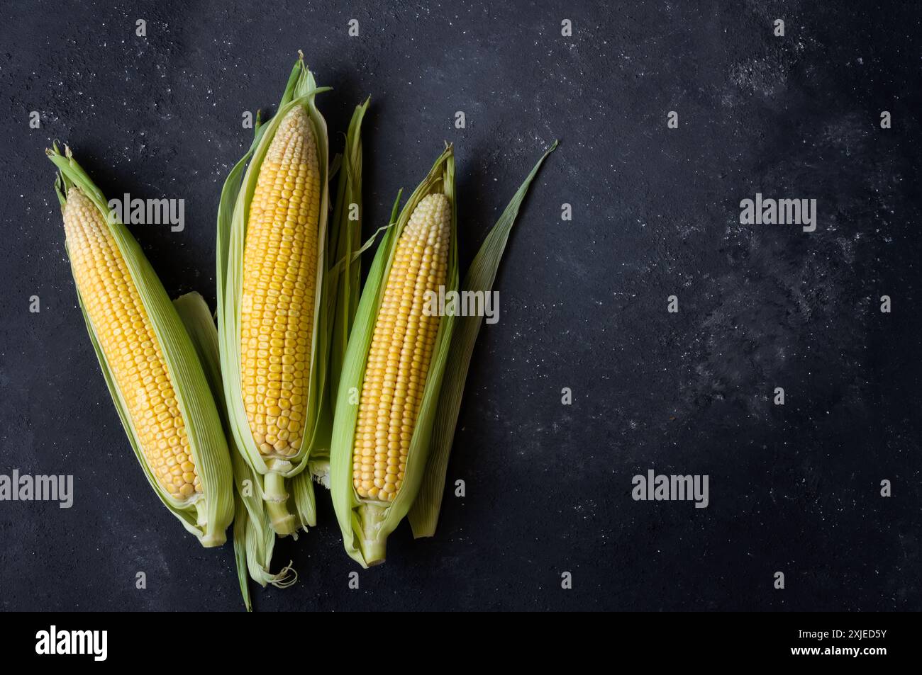 Fresh ripe three half peeled corn cobs on dark rustic table, grain ...