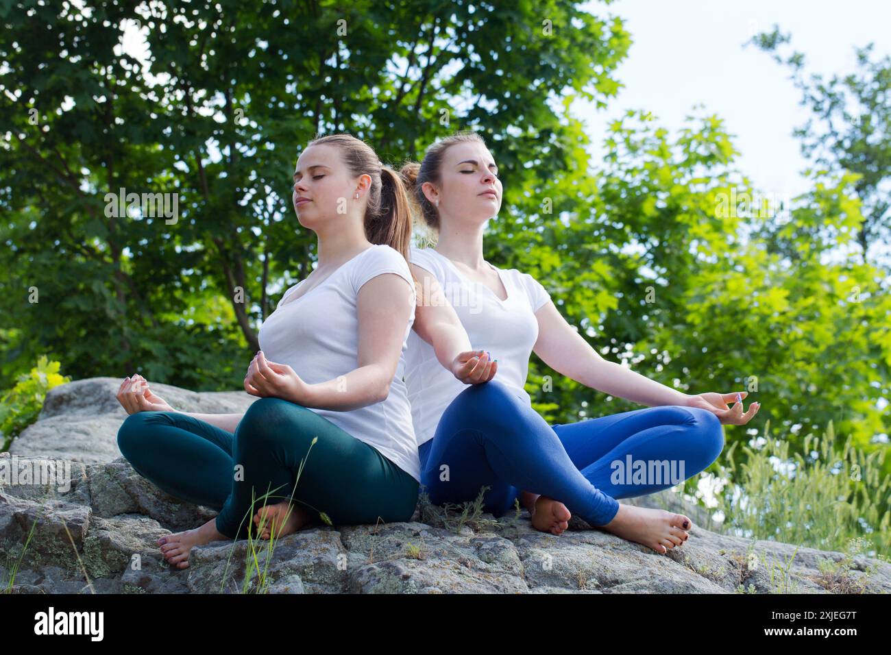 Two healthy calm young women meditating in nature with eyes closed ...