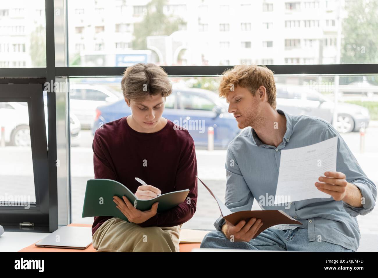 Two male students seated on a bench, engaged in studying papers ...