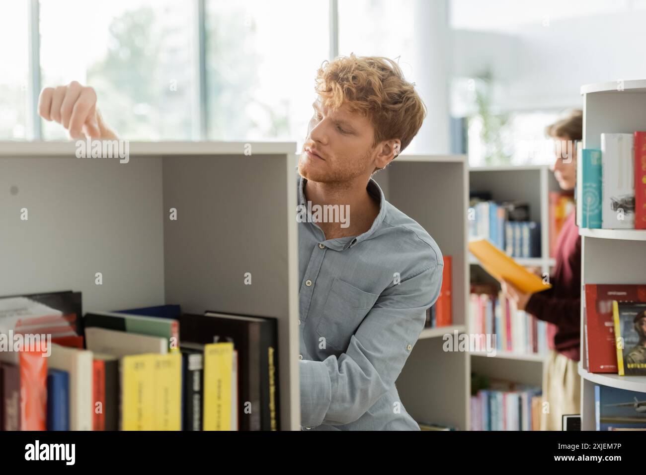 A man casually leaning against a bookshelf in a library, with his ...