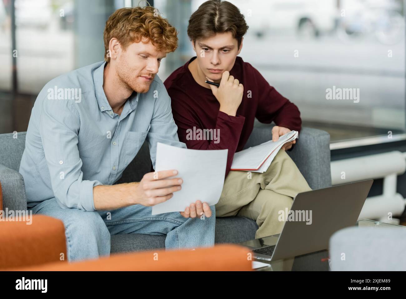 Two men focus on a paper while sitting on a couch Stock Photo - Alamy