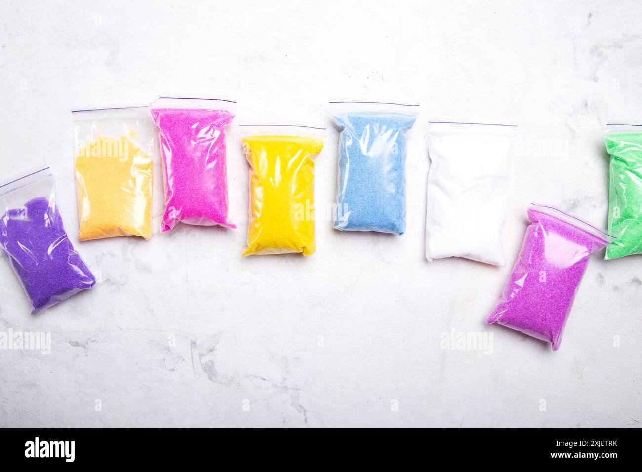 Vibrant spectrum of colored sand in clear plastic bags on marble ...