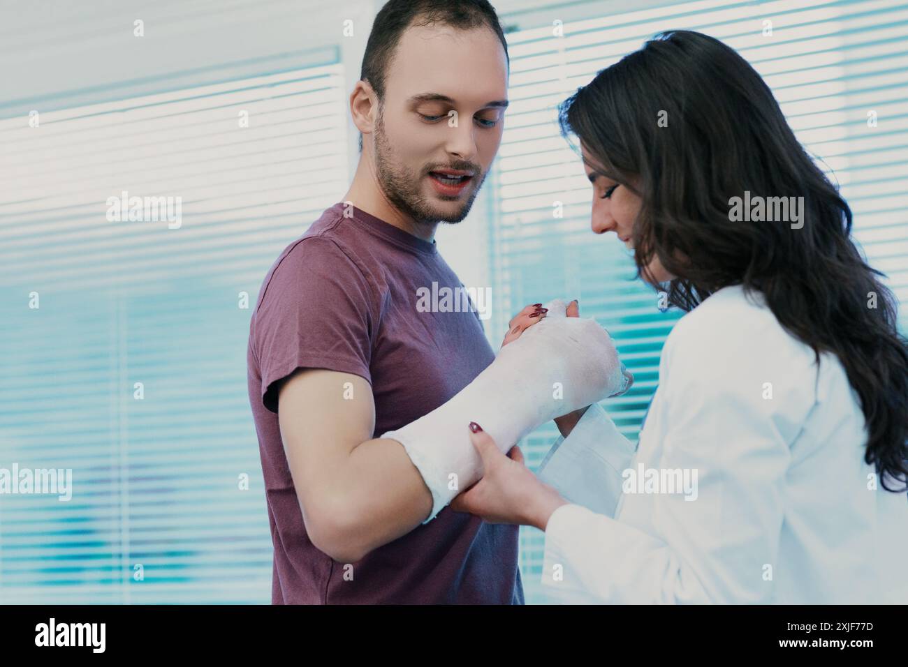 Doctor is carefully examining the arm cast of a young man in a medical ...
