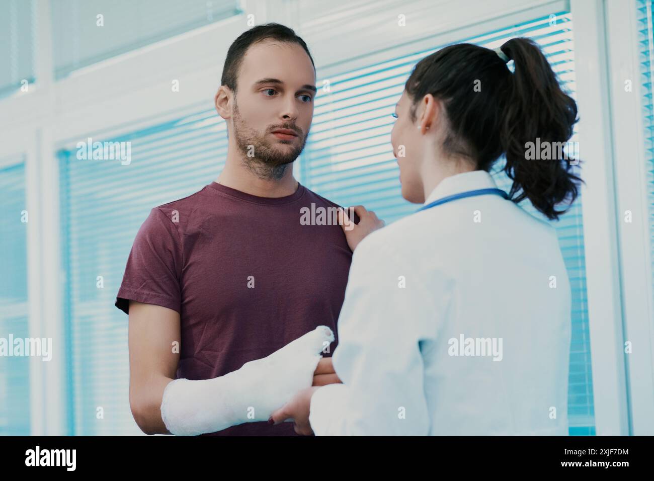Caring doctor comforts a worried patient with an arm cast in a bright ...