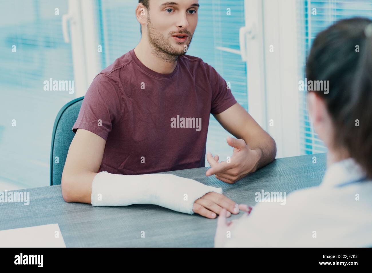 Young man with his arm in a cast sits across from a doctor, actively ...