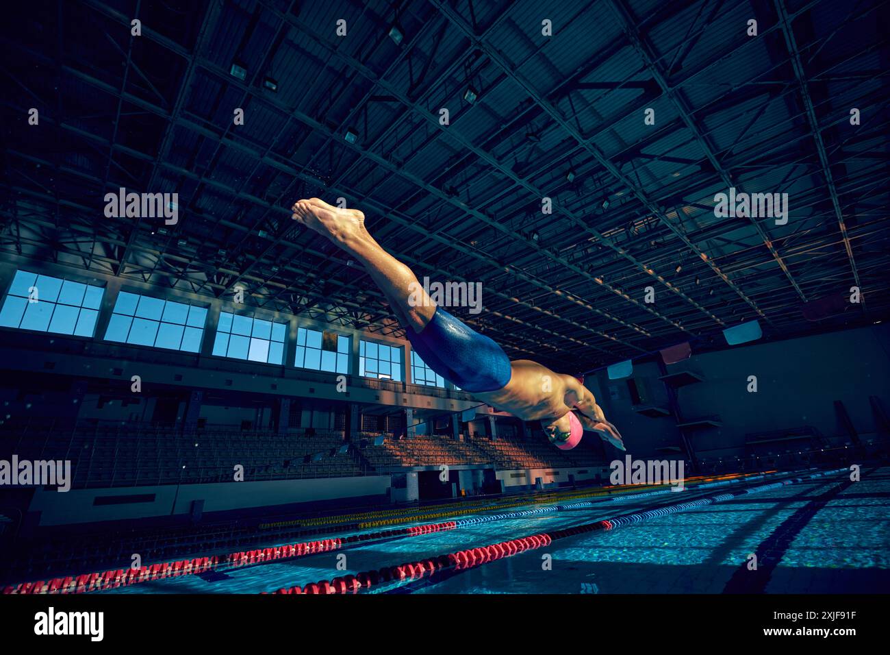 Swimmer in pink cap and blue trunks dives gracefully into indoor pool ...