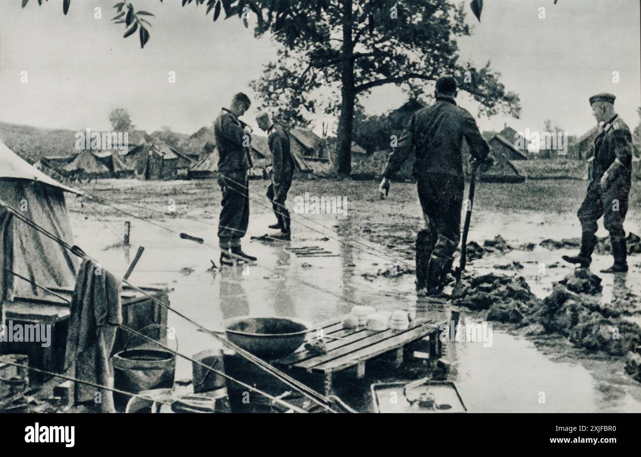 A photograph shows German soldiers dealing with a flooded camp after a ...