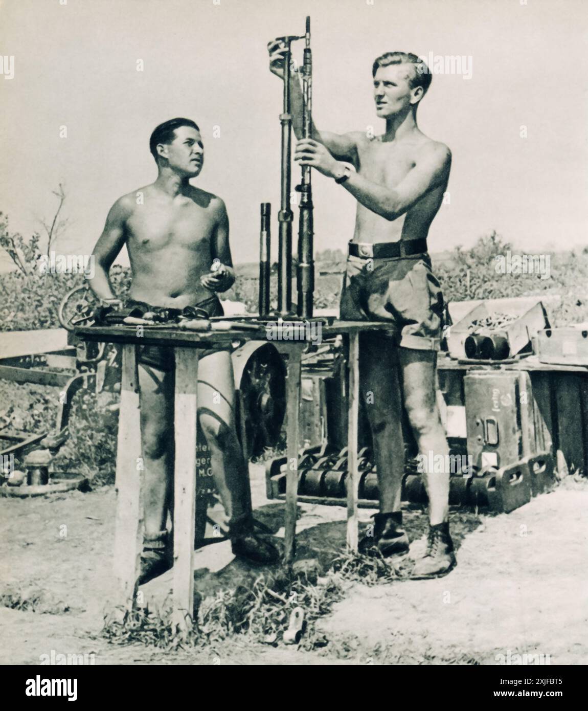 A photograph shows two German soldiers at a bench adjusting the machine ...