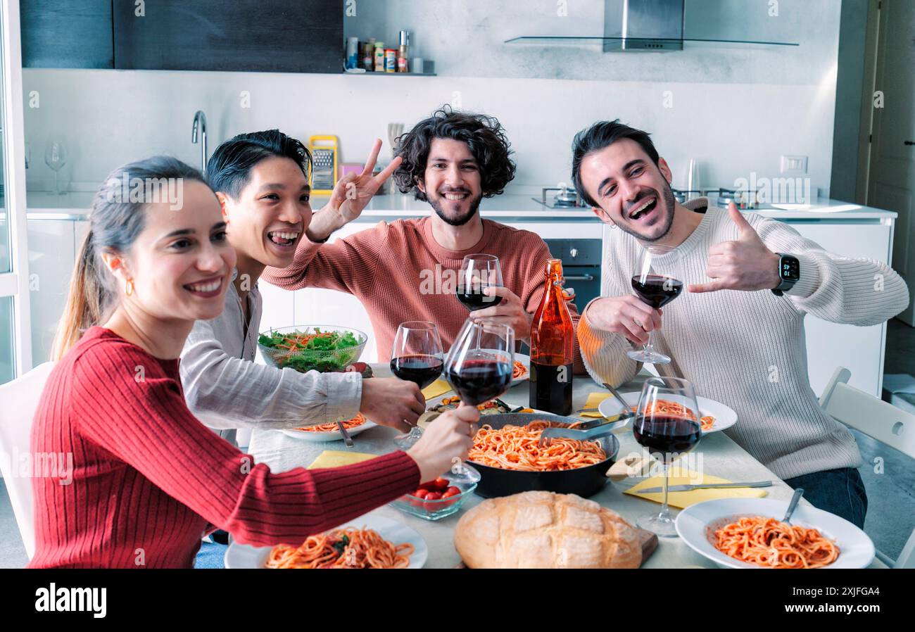 Happy ethnic group of friends eating pasta and drinking wine at home ...