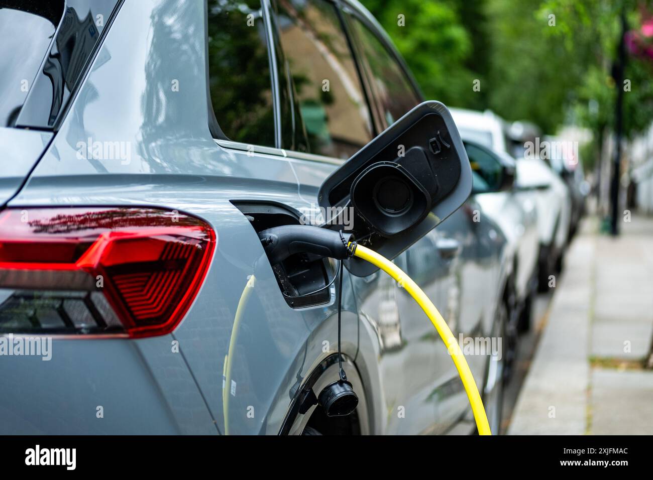 An electric car plugged in on charge on a residential street in central ...