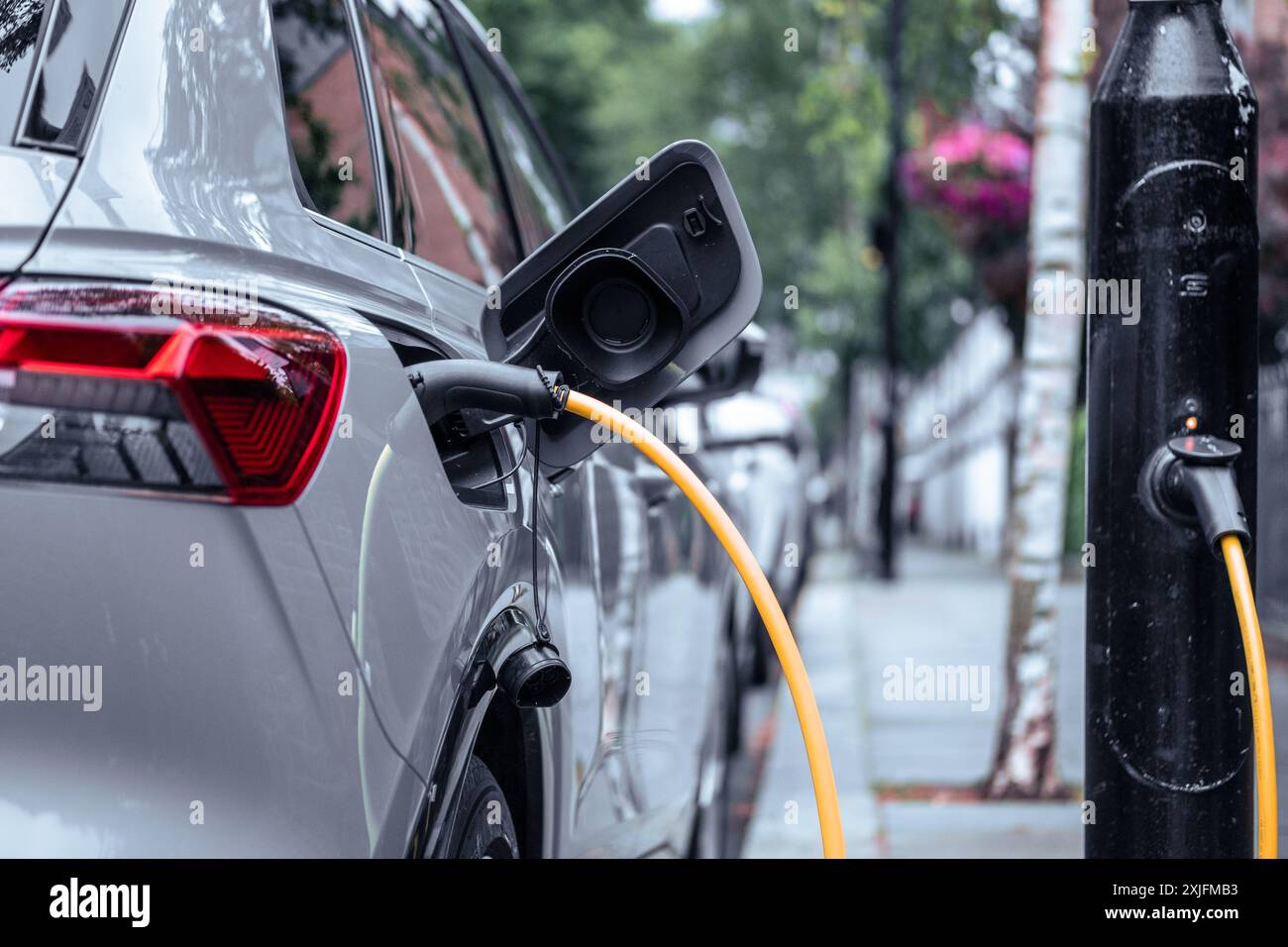 An electric car plugged in on charge on a residential street in central ... An electric car plugged in on charge on a residential street in central ...