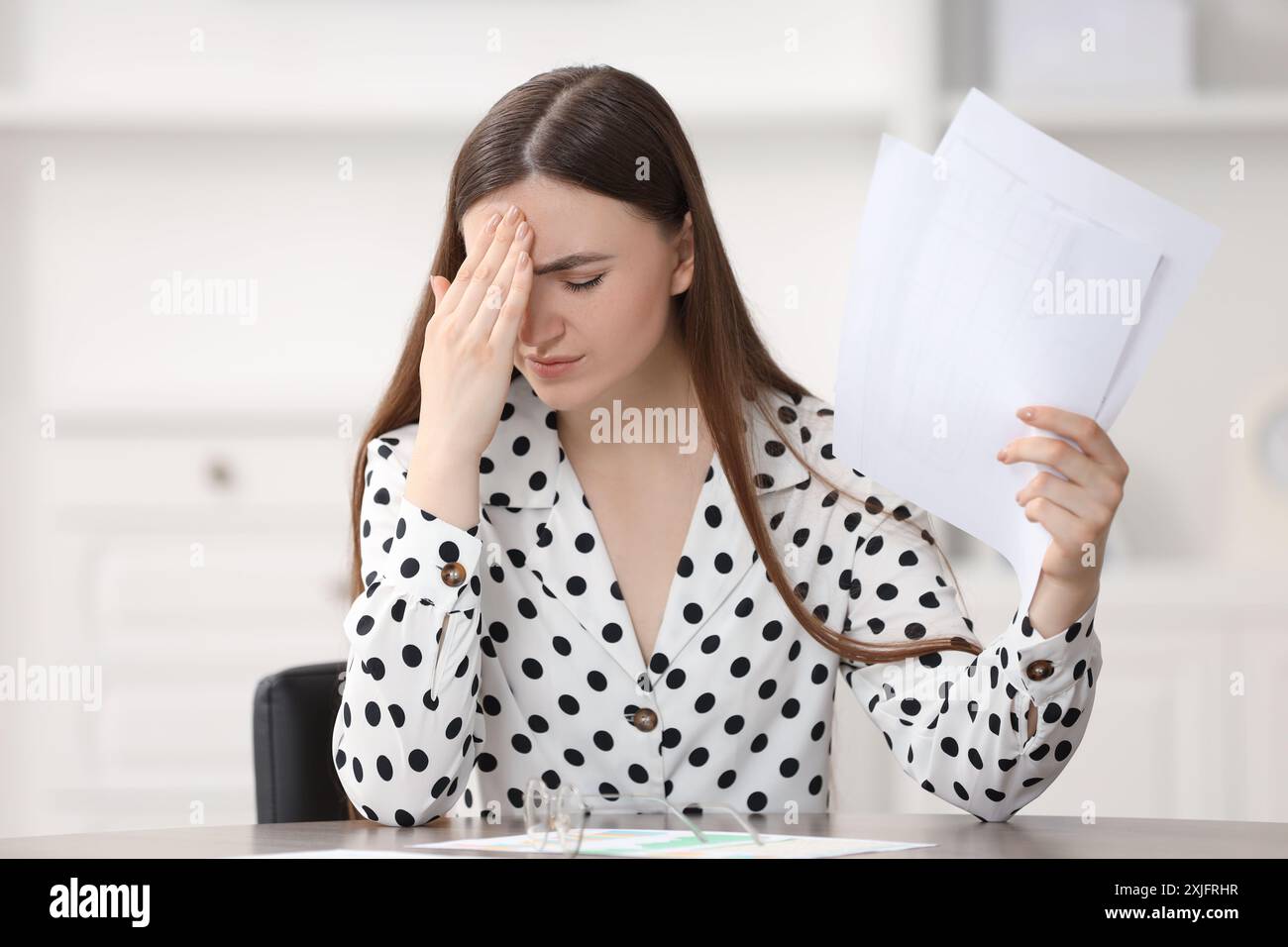 Embarrassed woman with documents at table in office Stock Photo - Alamy