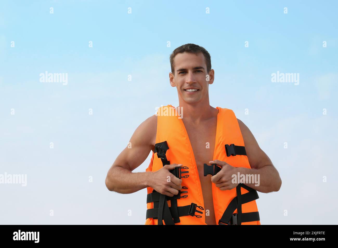 Handsome lifeguard putting on life vest against sky Stock Photo - Alamy