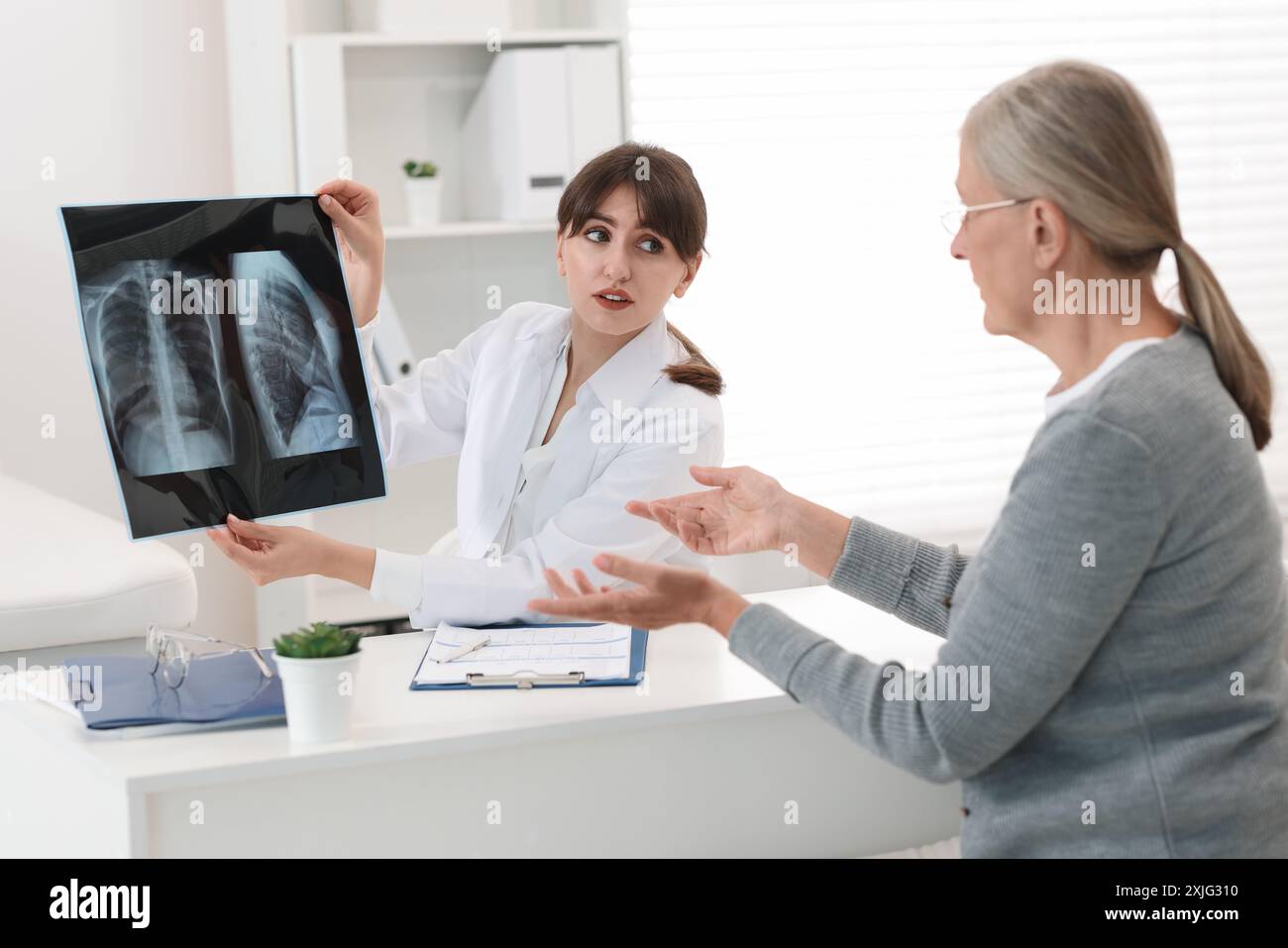 Lung disease. Doctor showing chest x-ray to her patient at table in ...