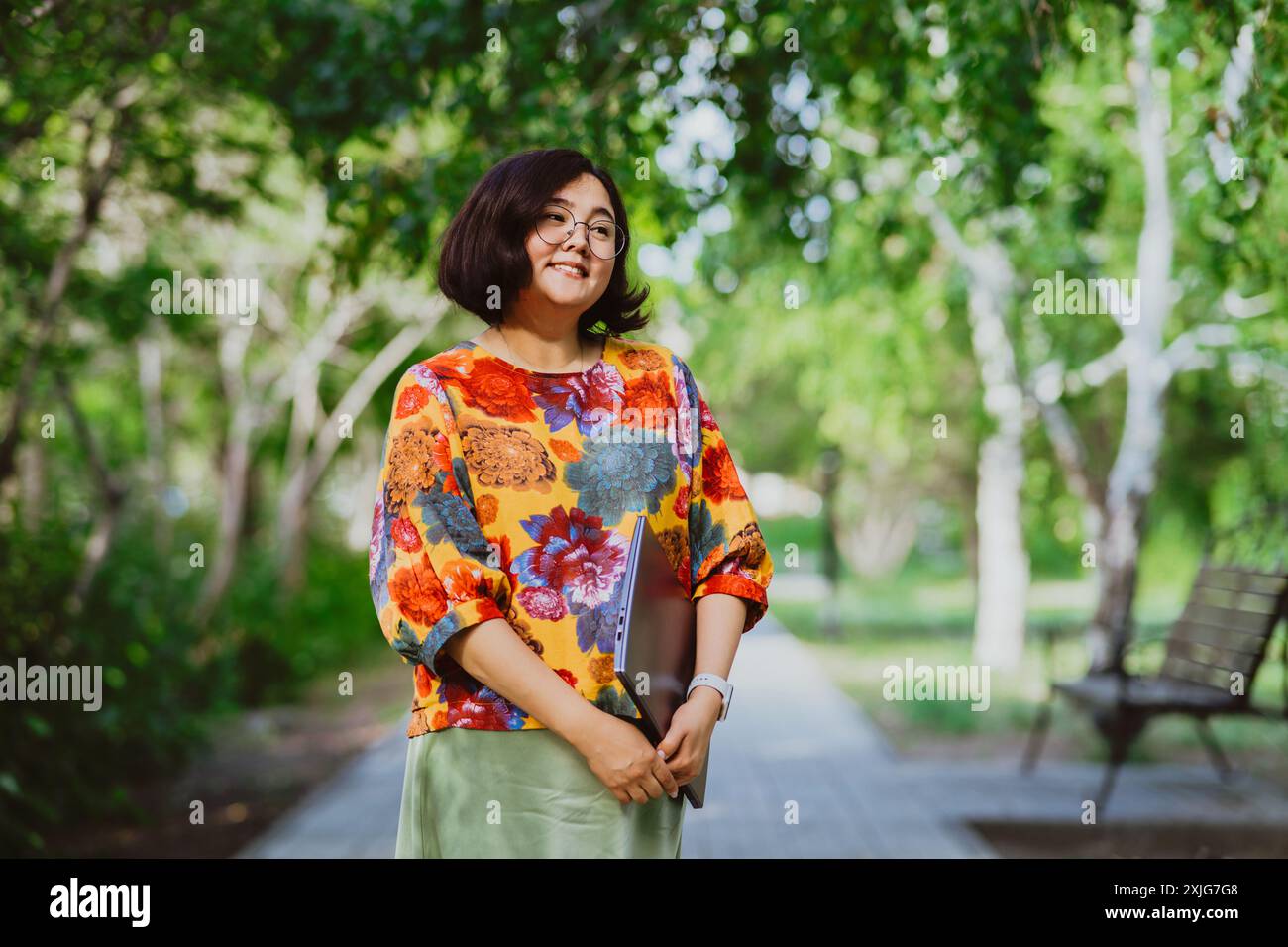 A fashionable, smiling Asian woman hugging a laptop is walking in the ...